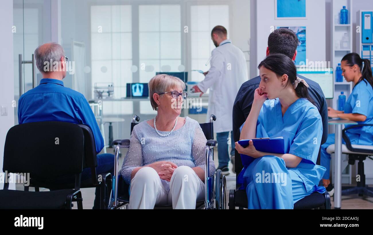Nurse filing documents while talking with disabled senior woman in ...