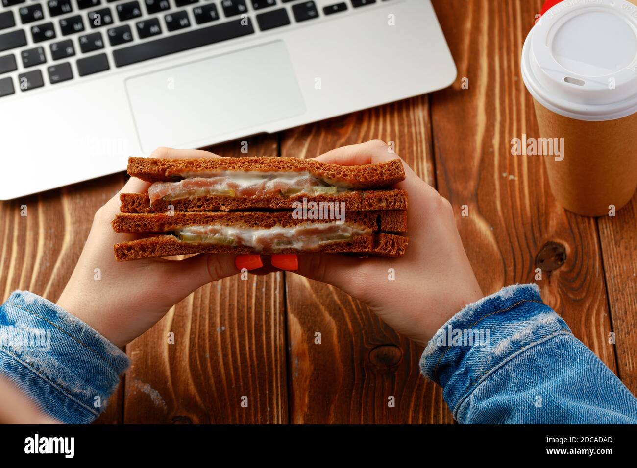 Hands of a woman holding sandwich above working table with laptop Stock ...