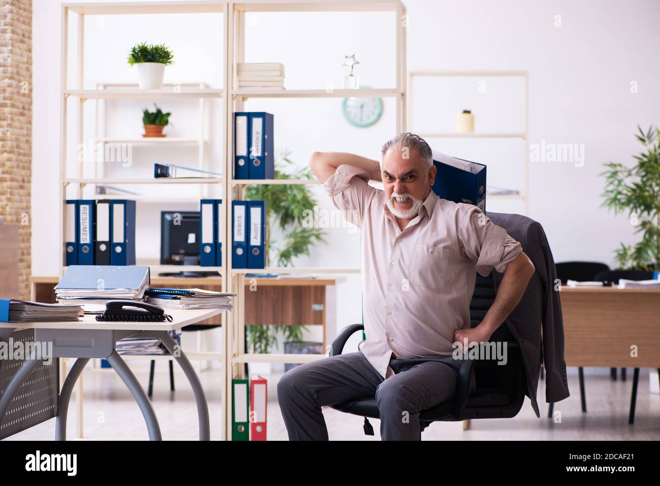 Senior male employee doing physical exercises at workplace Stock Photo ...