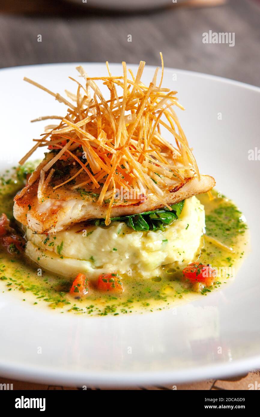 Steamed fish with mashed potatoes cheese tomatoes and sauce on a white ...