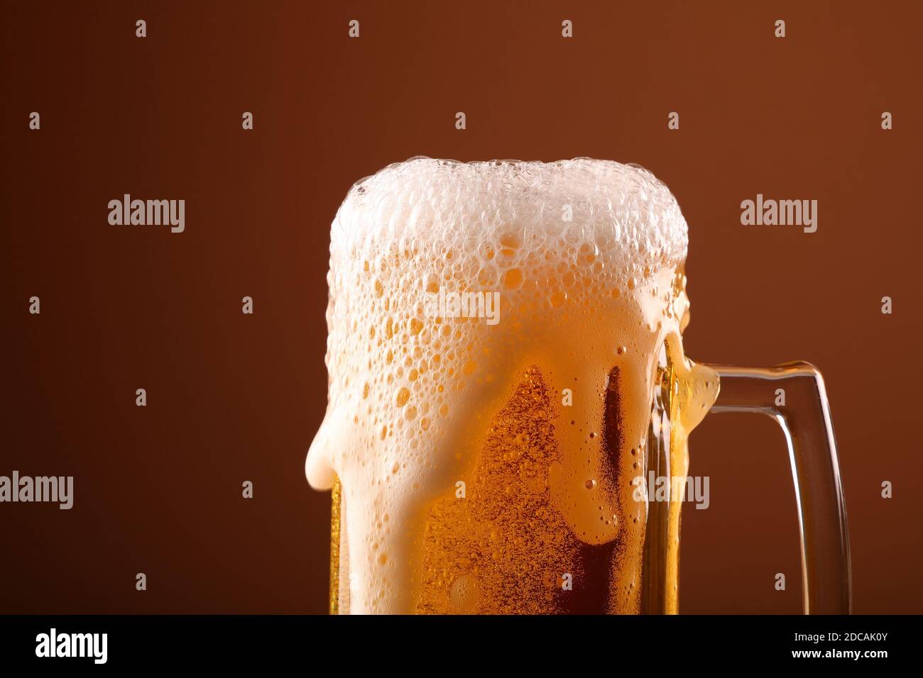 Close up pouring lager beer with white froth and bubbles in glass mug ...