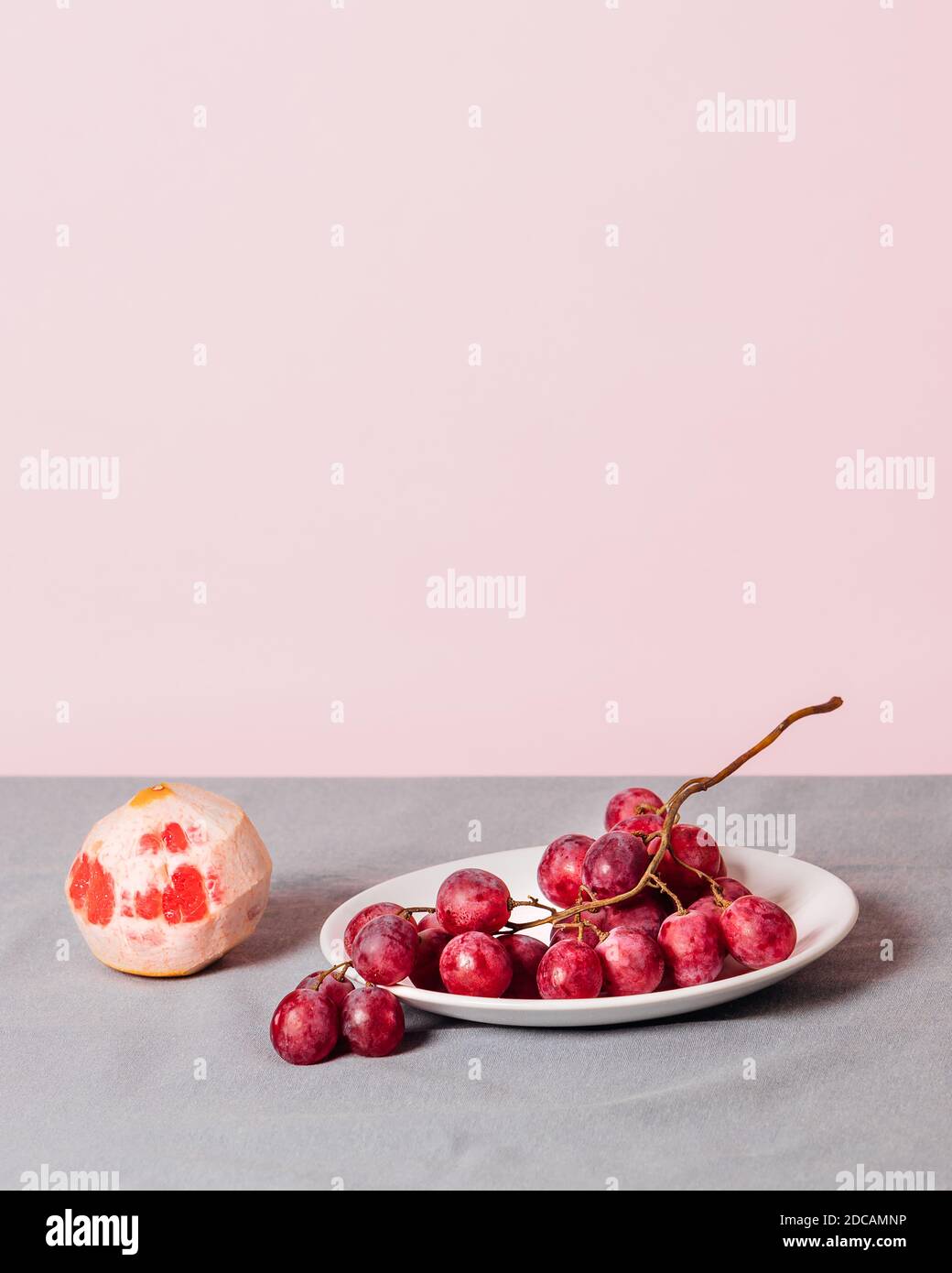 Close-up of a bunch of grapes and a peeled grapefruit on a pink ...