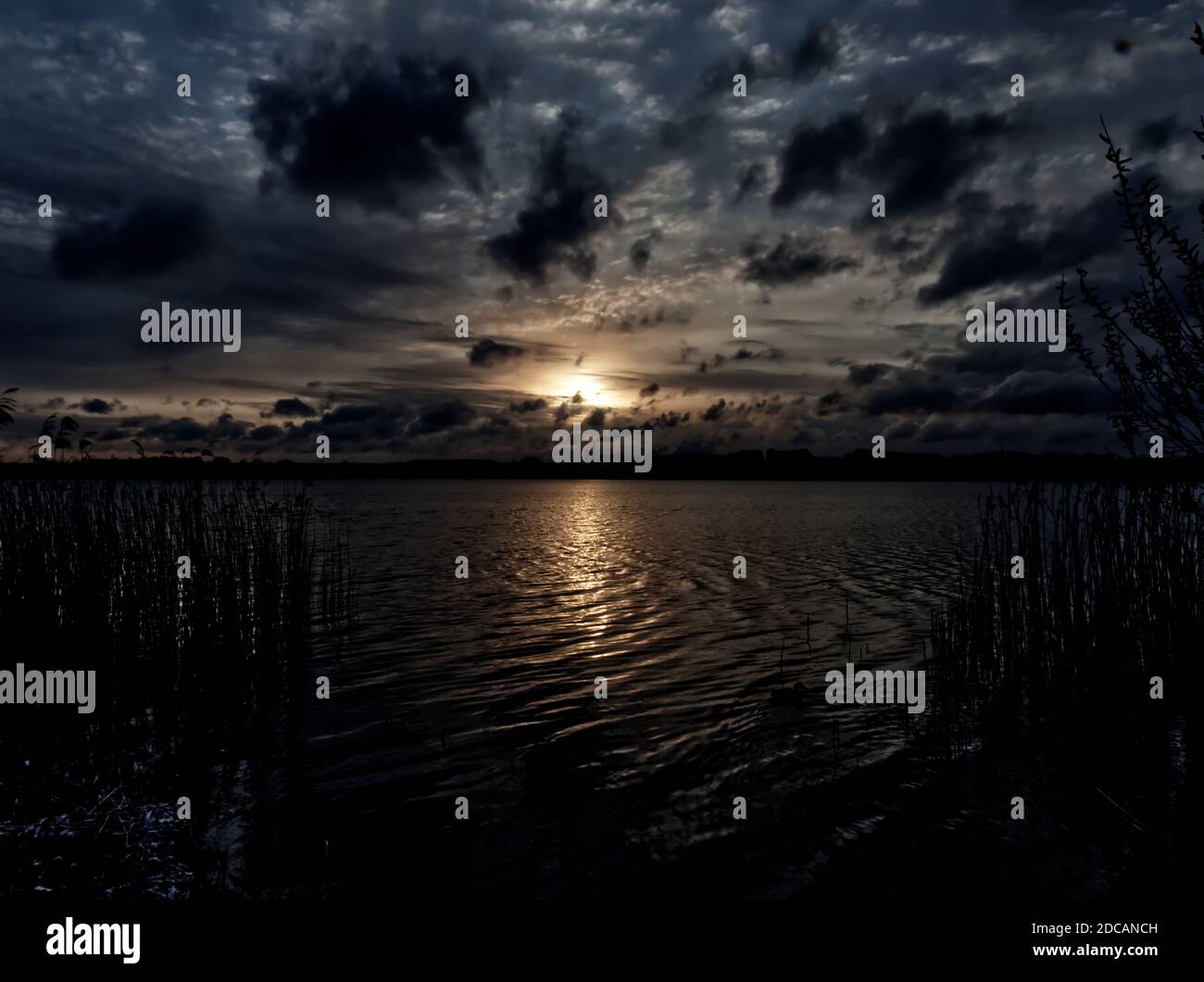 Underexposed view at the lake with a rising sun and industrial ...