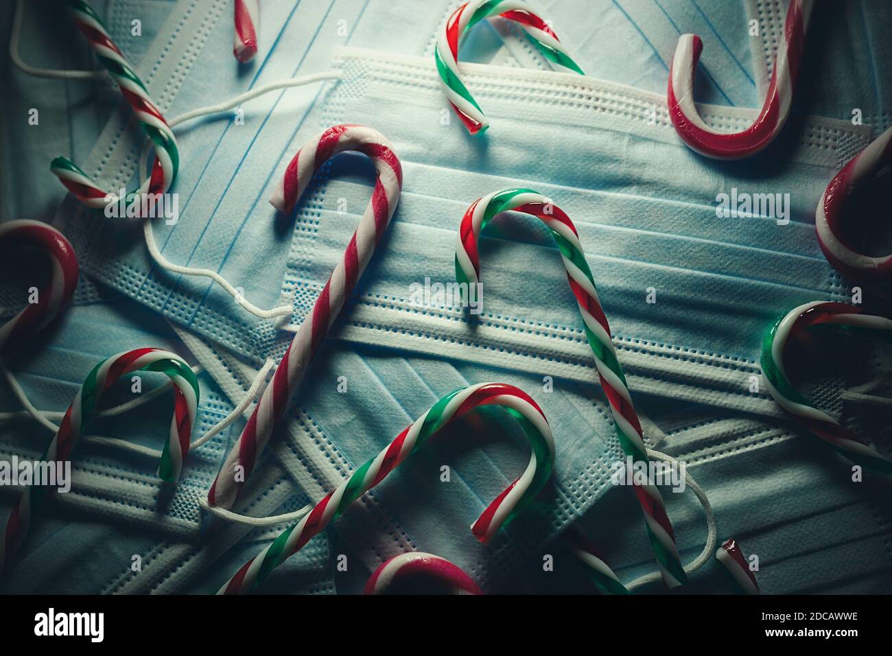 Blue medical face masks and candy canes on top of them, in dark with ...