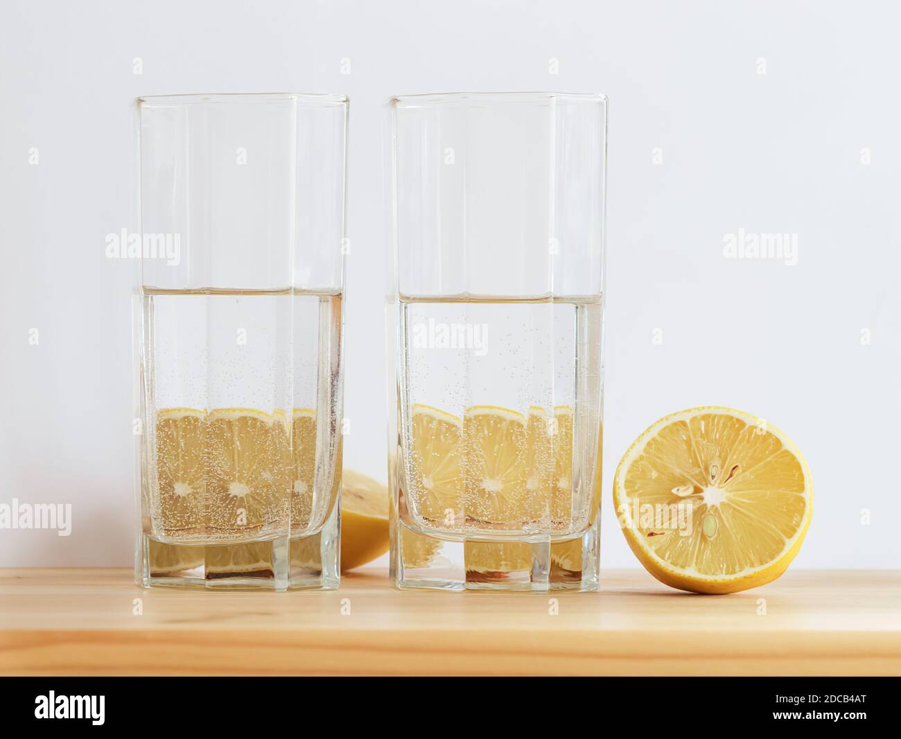 Glass of water and cut lemon are standing on the wooden desk. White ...
