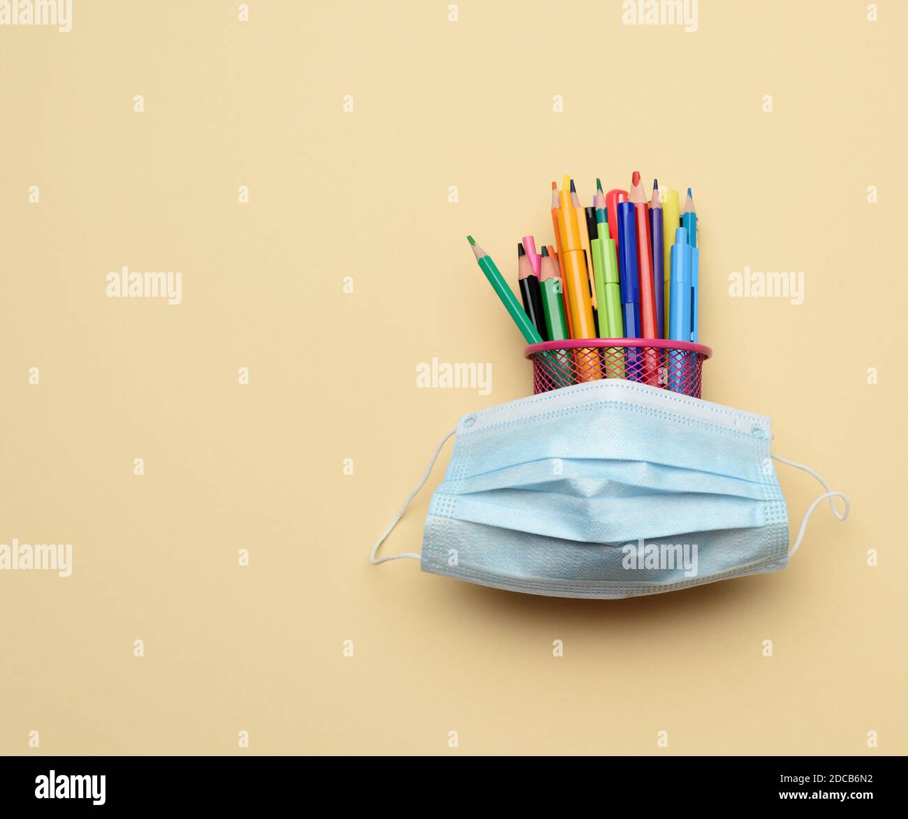 disposable medical mask and multi-colored pencils and pens in a metal ...
