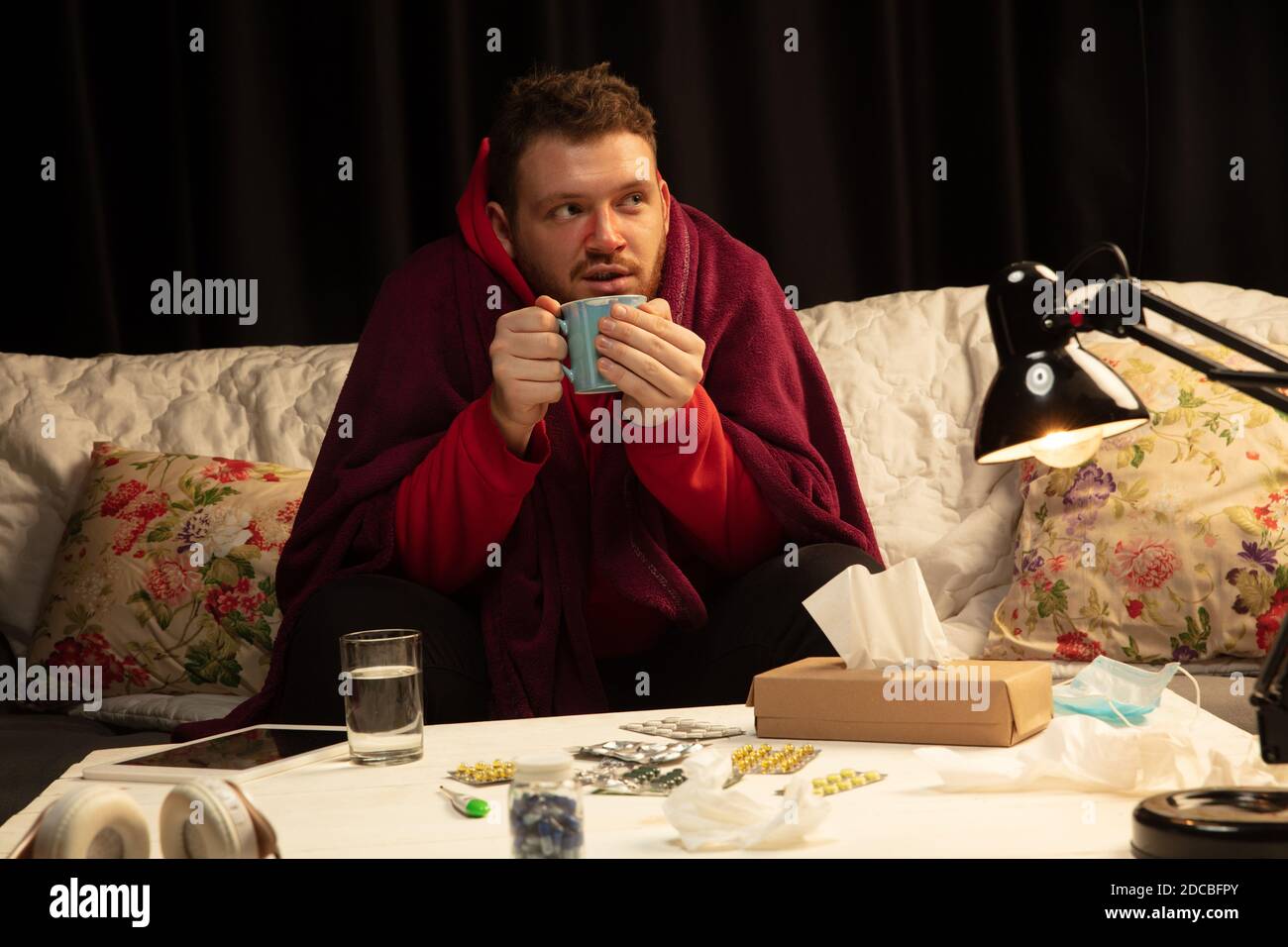 Fever. Young man wrapped in a plaid looks sick, ill, sneezing and ...