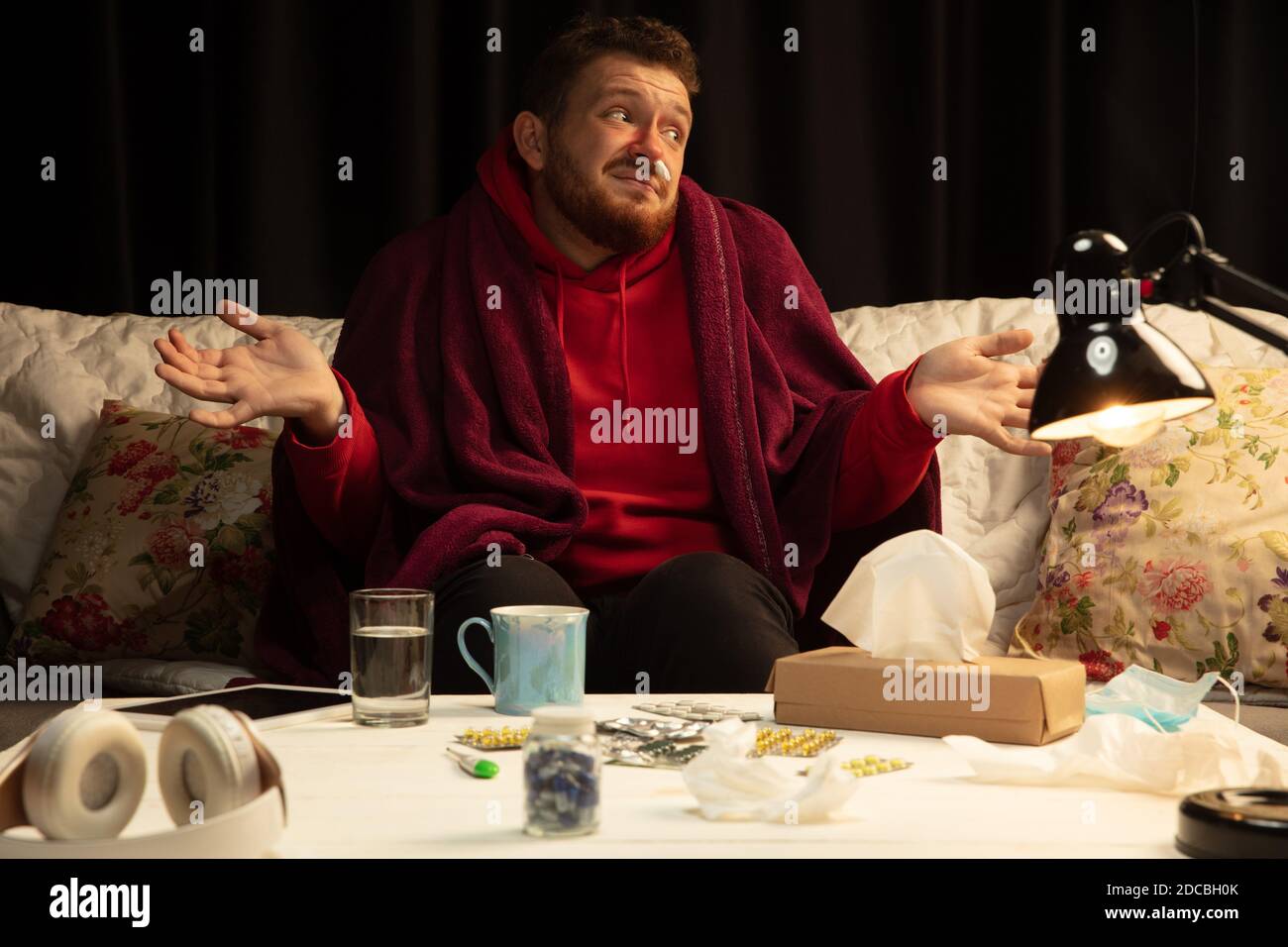 Rainy nose. Young man wrapped in a plaid looks sick, ill, sneezing and ...