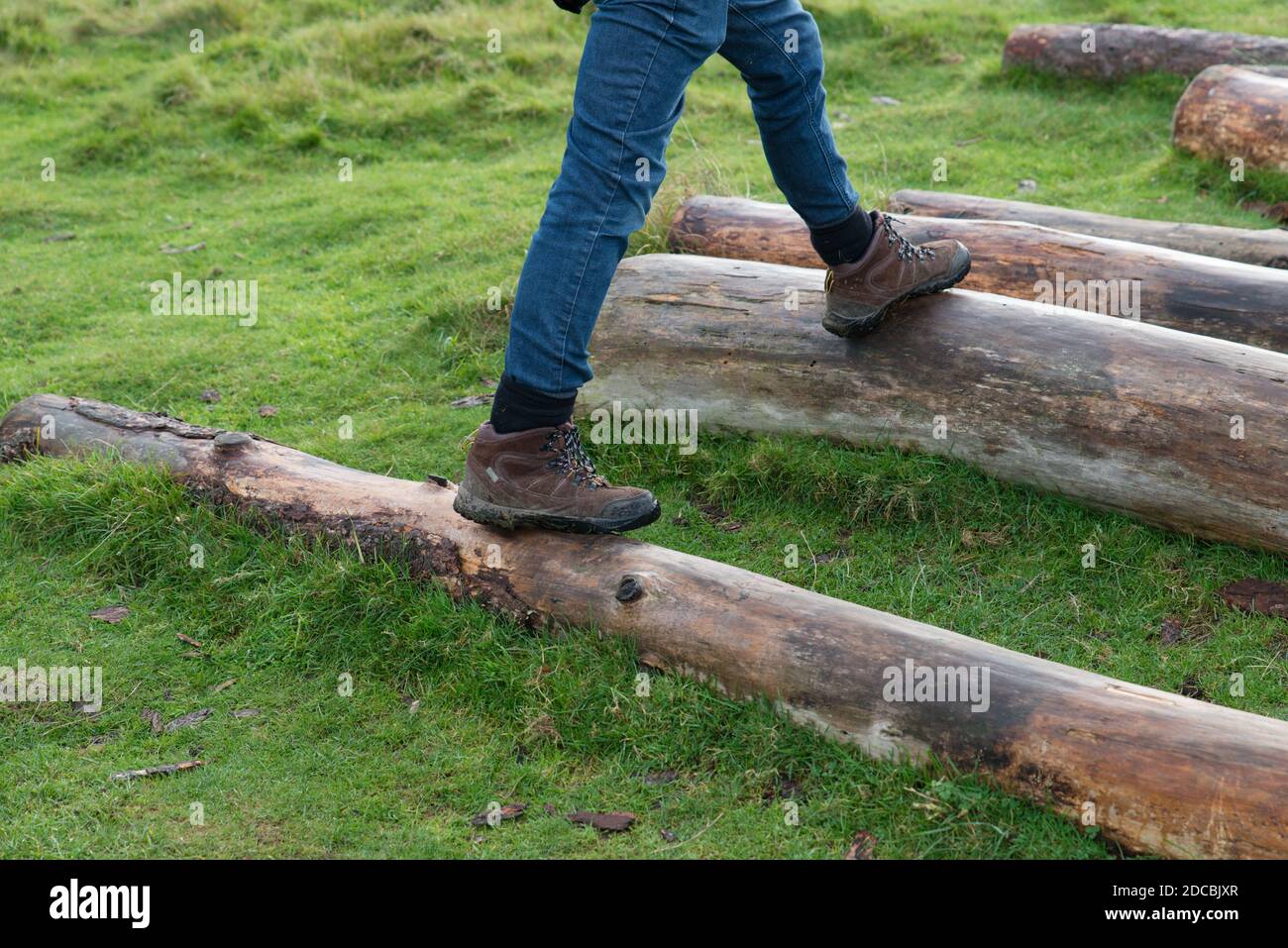 close up of man's legs and feet stepping on wooden tree trunk logs ...
