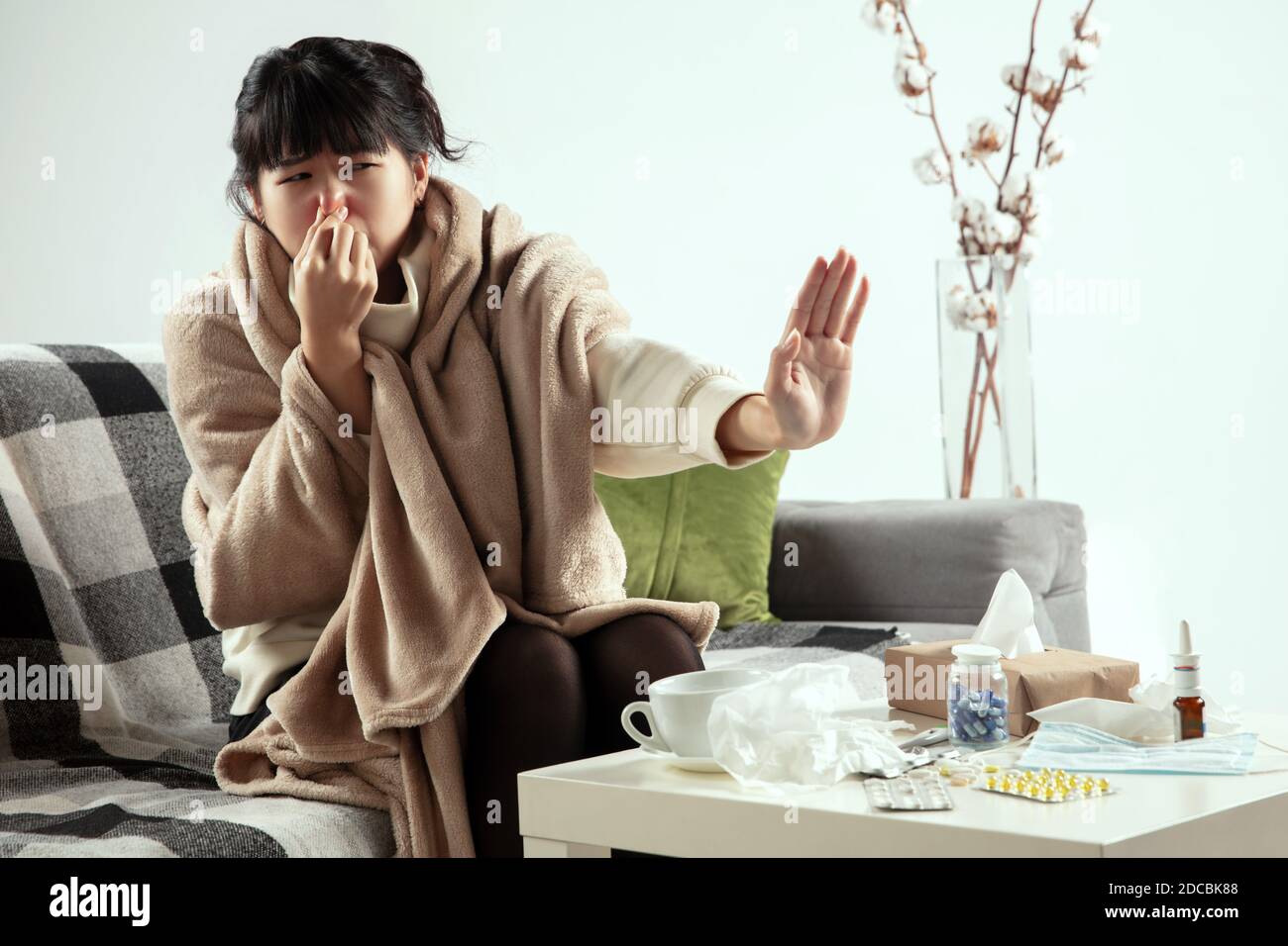 Rainy nose. Young woman wrapped in a plaid looks sick, ill, sneezing ...