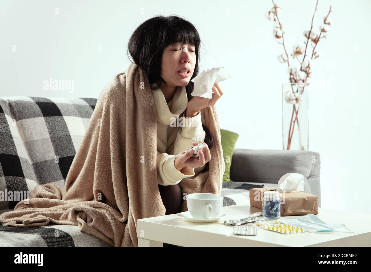 Rainy nose. Young woman wrapped in a plaid looks sick, ill, sneezing ...