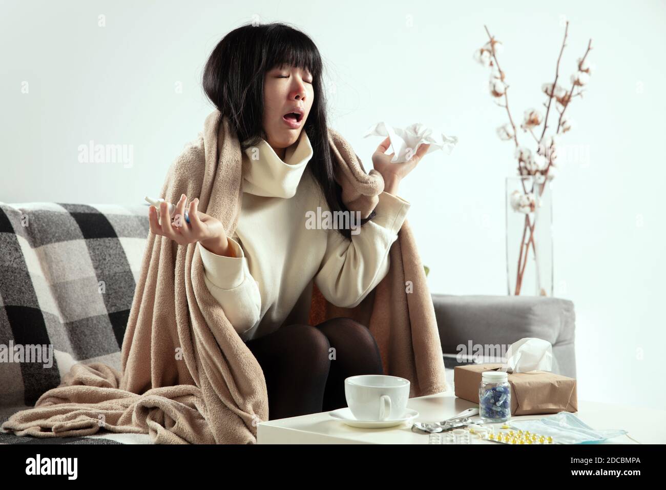 Rainy nose. Young woman wrapped in a plaid looks sick, ill, sneezing ...