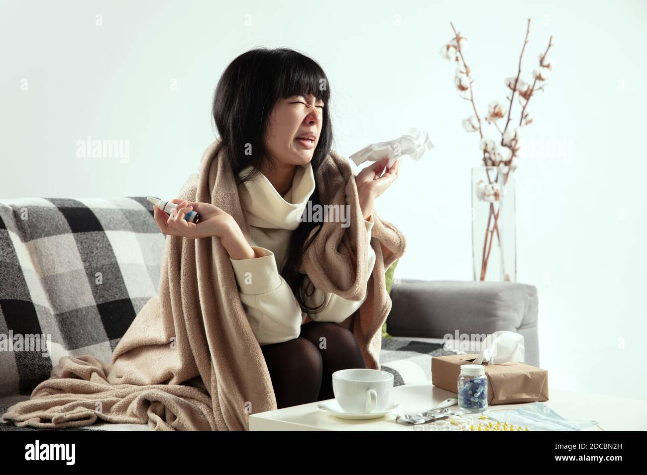 Rainy nose. Young woman wrapped in a plaid looks sick, ill, sneezing ...