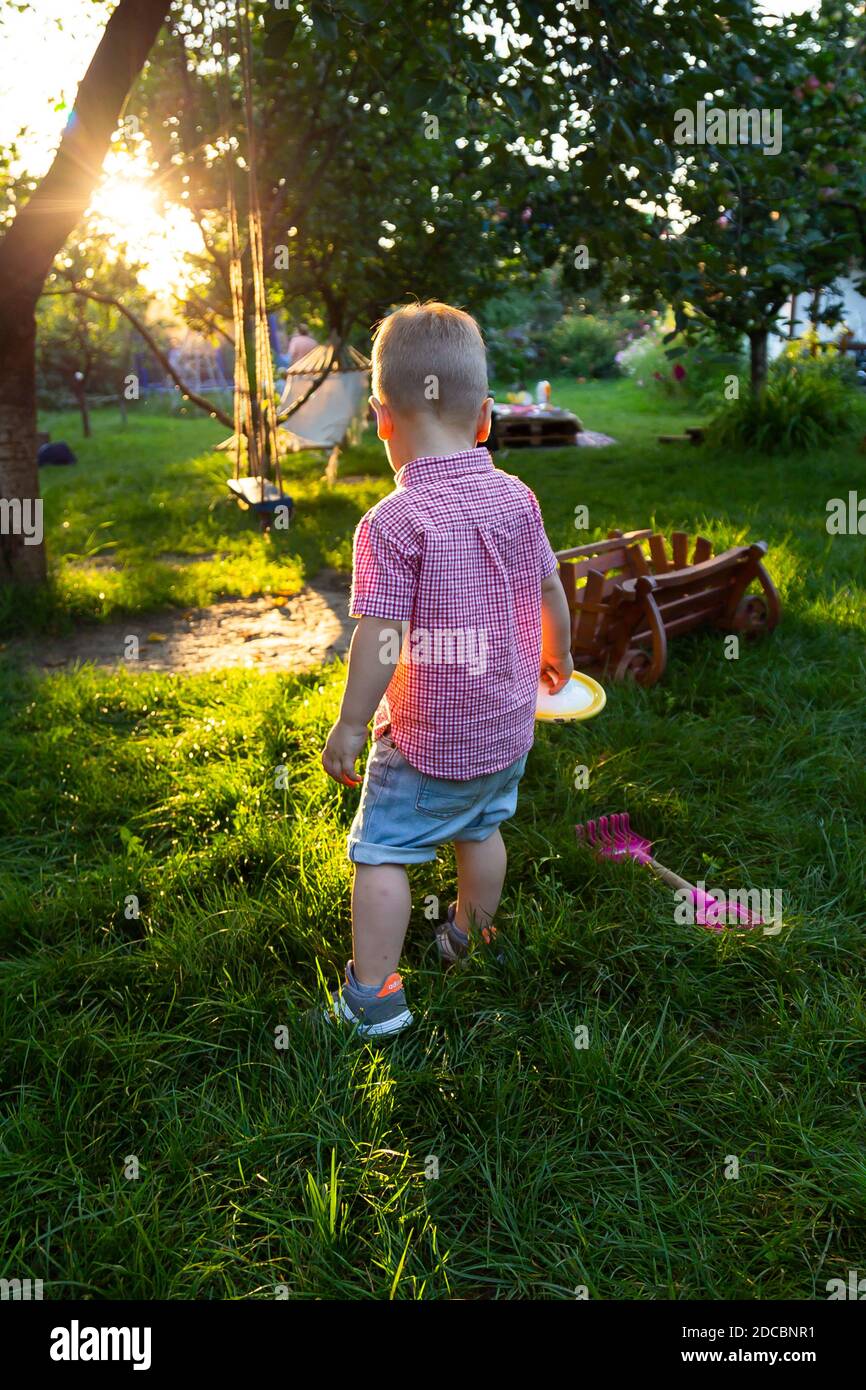 A back view of a cute blond baby boy playing in a grassy summer park ...