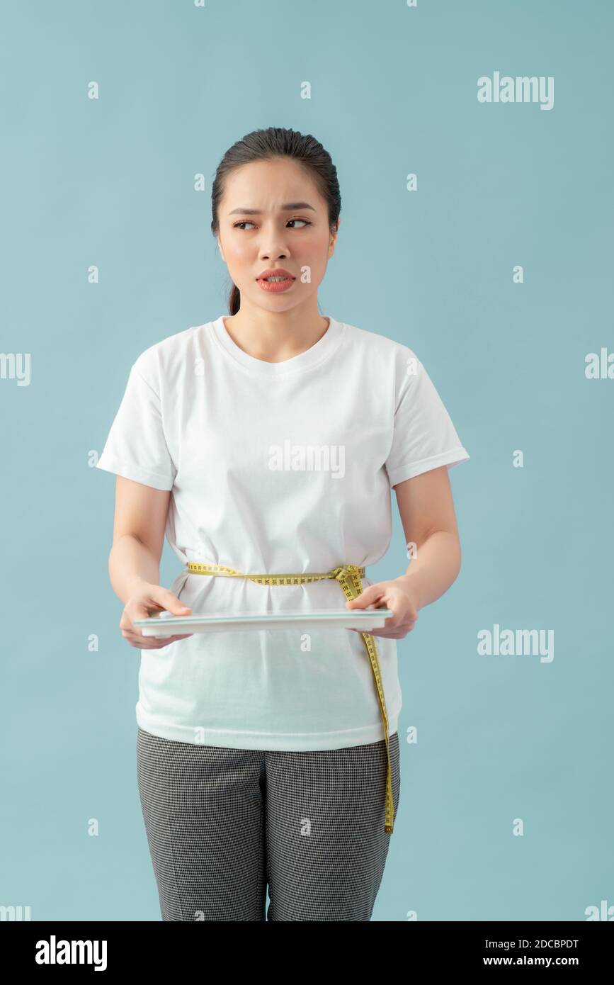 A asian woman holding scales with a tape measure around her belly on a ...