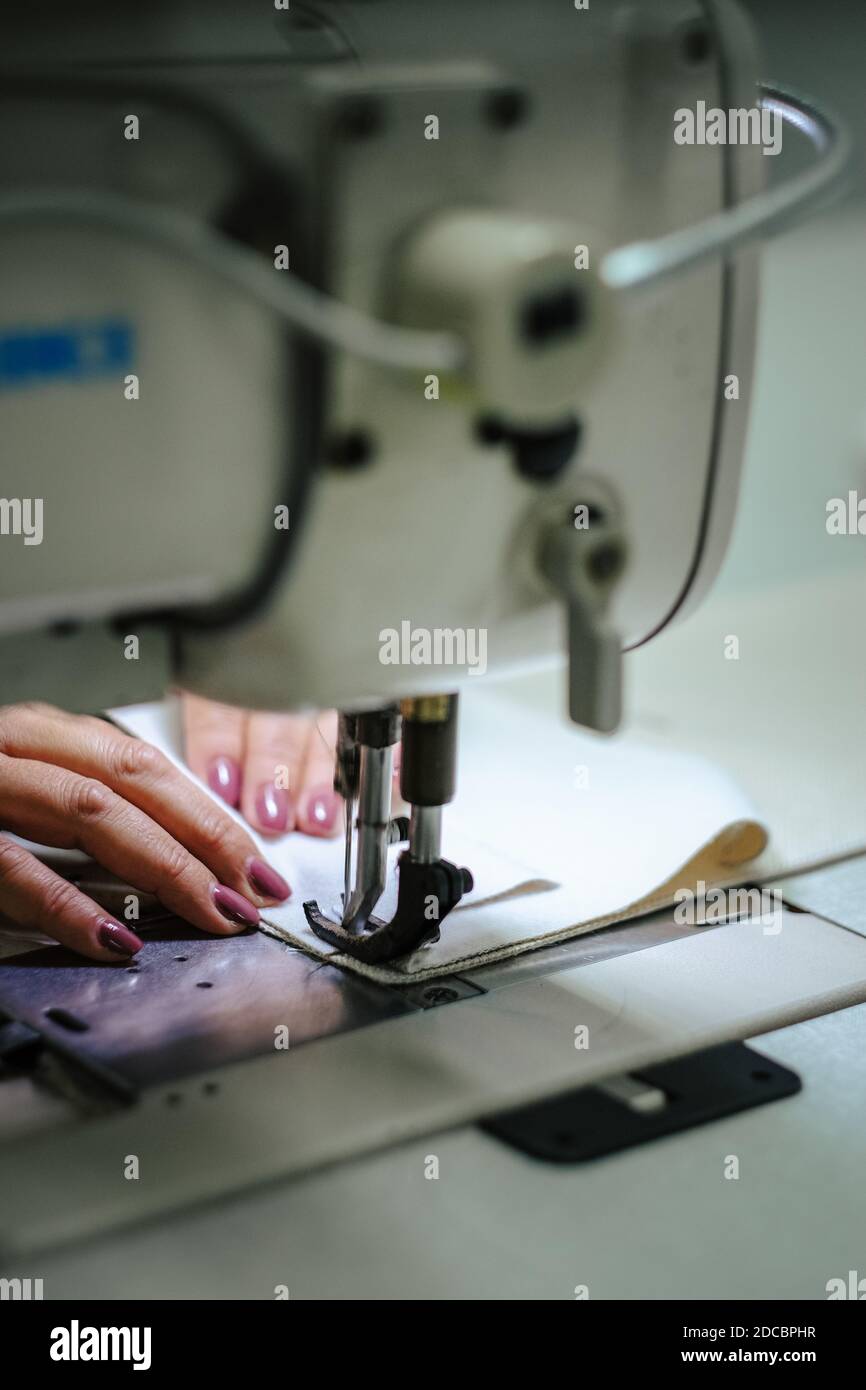 A vertical closeup shot of female hands operating an industrial sewing ...