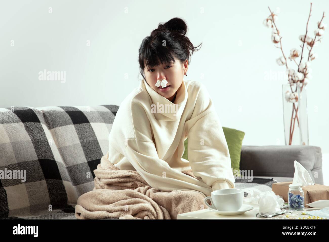 Shiver. Young woman wrapped in a plaid looks sick, ill, sneezing and ...