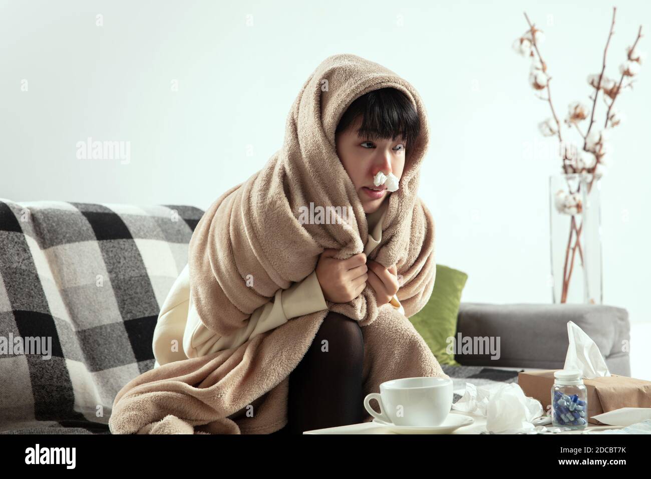 Shiver. Young woman wrapped in a plaid looks sick, ill, sneezing and ...