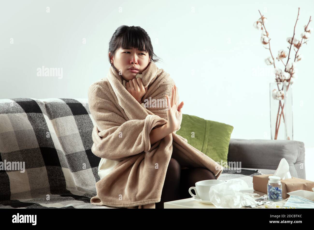 Shiver. Young woman wrapped in a plaid looks sick, ill, sneezing and ...