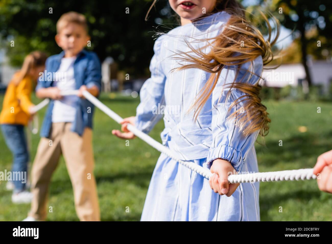 Girl holding rope while playing tug of war with friends on blurred ...