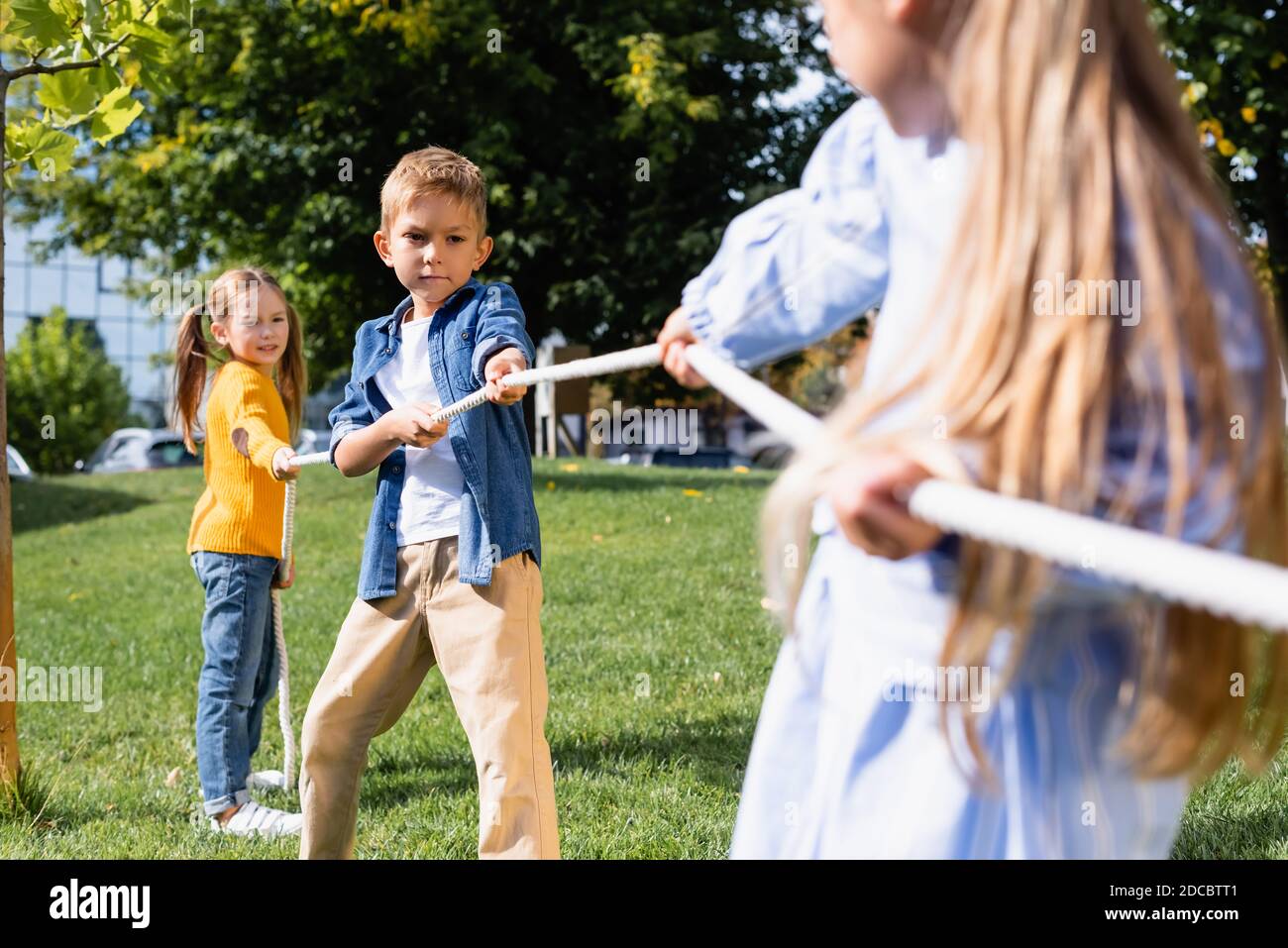 Boy pulling rope while playing tug of war with friends on blurred ...