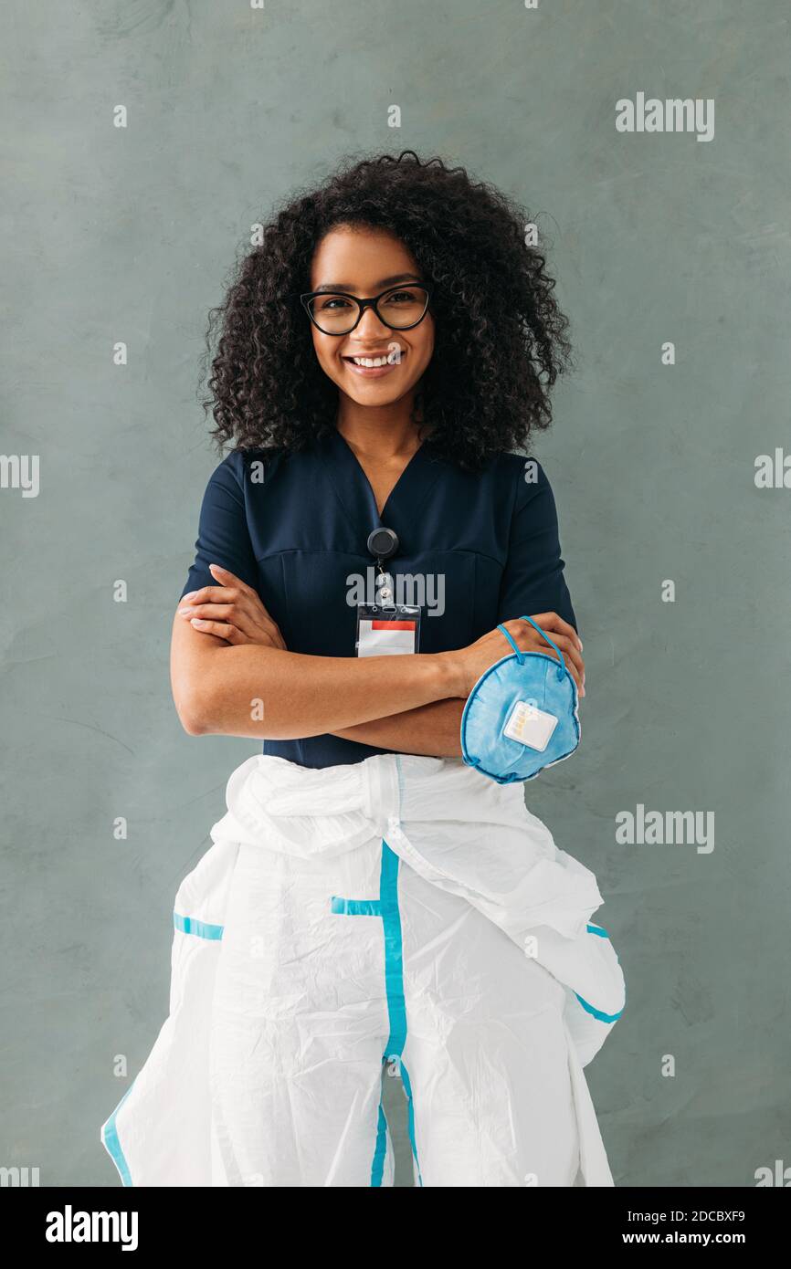 Smiling nurse standing at wall with crossed arms and holding respirator ...