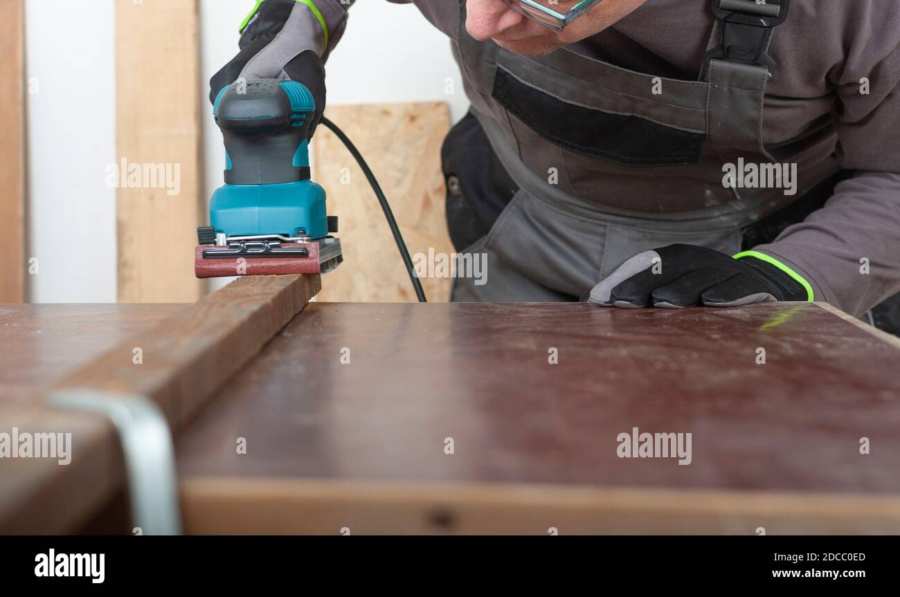 Carpenter working with electric sheet finishing sander on wood lath on ...