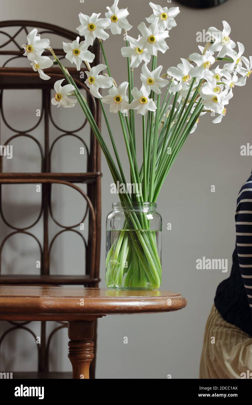 A bouquet of daffodils on the table indoors at home with woman sitting ...