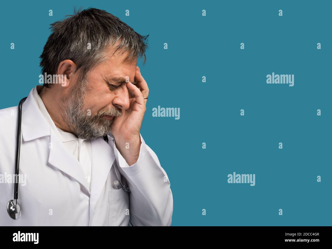 Portrait of a tired medical doctor with stethoscope against blue ...