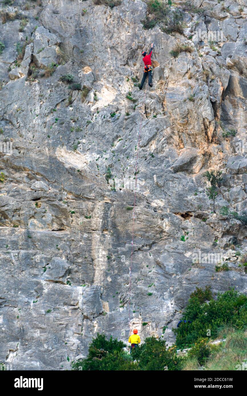 Two climbers, one climbing and the other securing, on a mountain with a ...