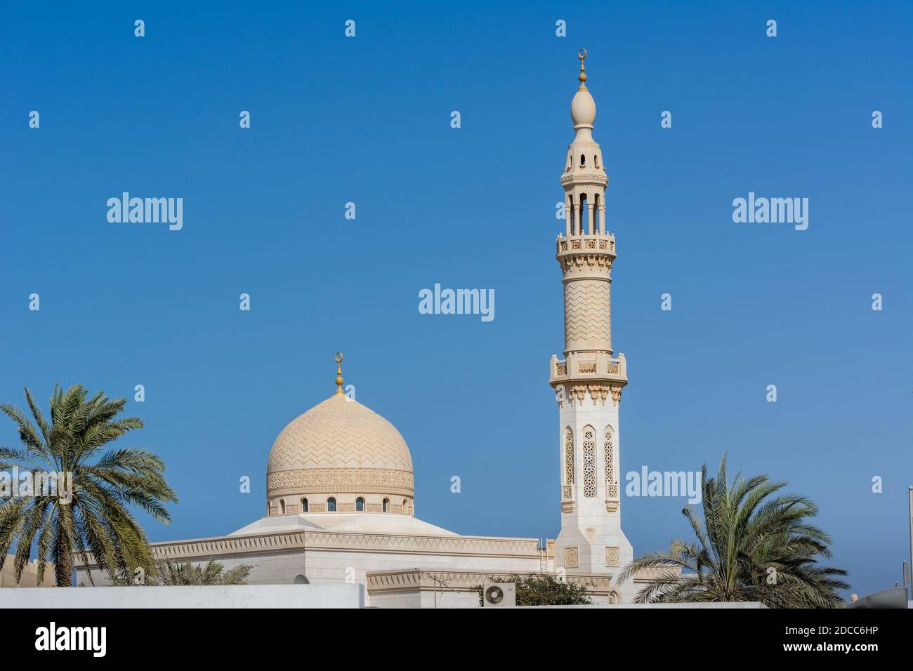The dome and minaret of Maharba mosque and palm tree against blue sky ...