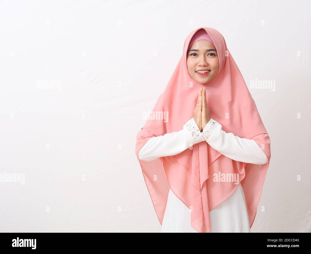 An Asian woman in Muslim dress stands up in a greetting pose to Namaste ...