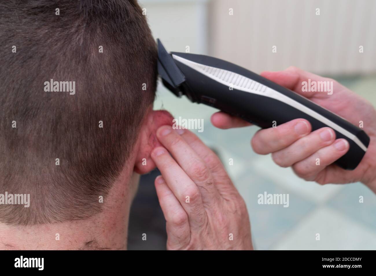 A close-up back view of someone using hair clippers on a teenage boy ...