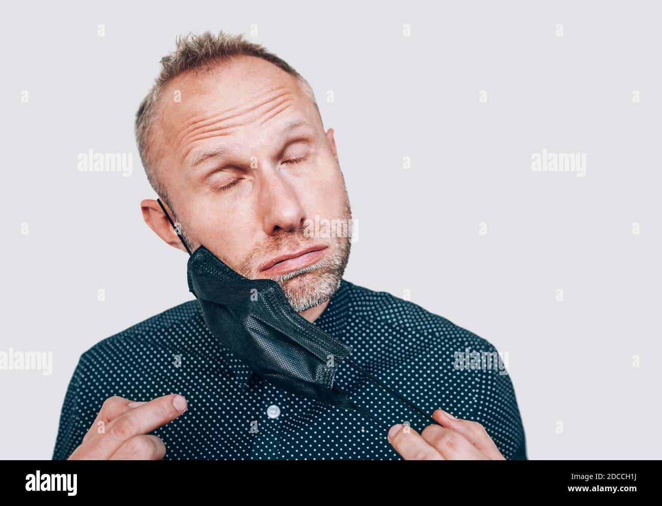 Portrait of tired man removing off a black facial mask during a COVID ...