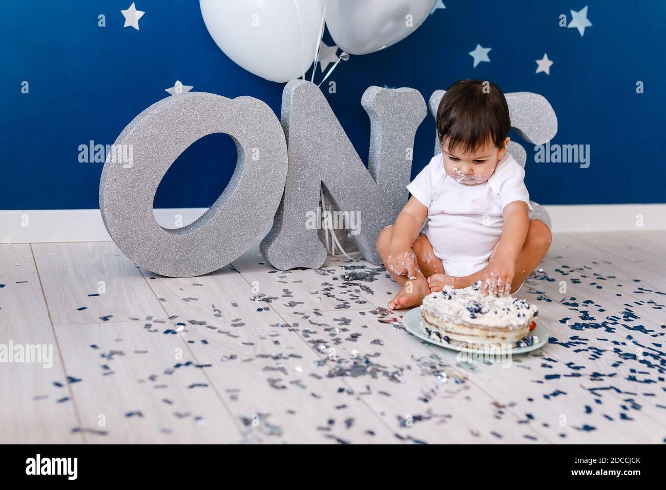 Curious baby boy poking finger in his first birthday cake on blue ...