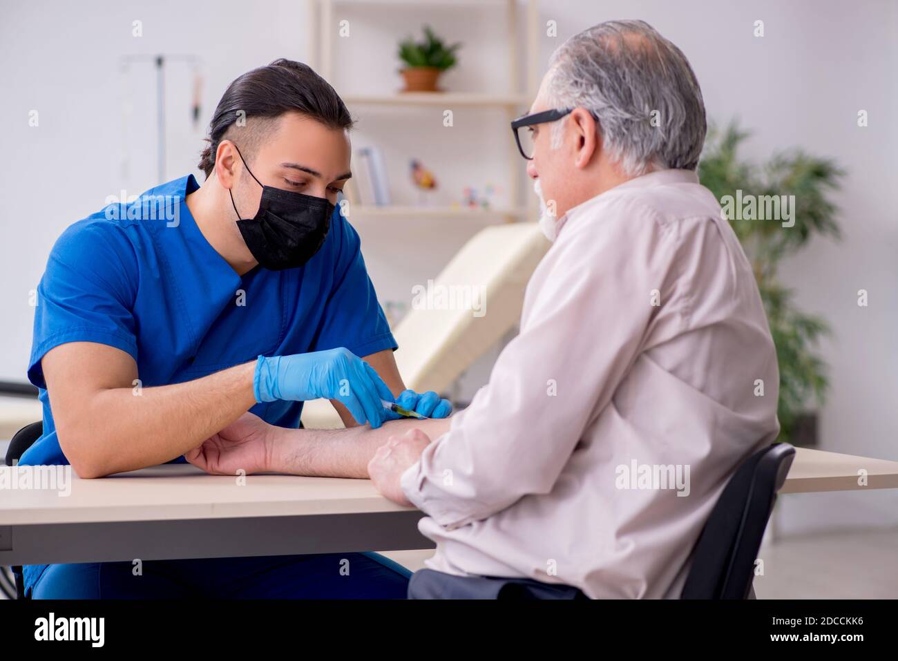 Old patient visiting young male doctor in blood transfusion concept ...