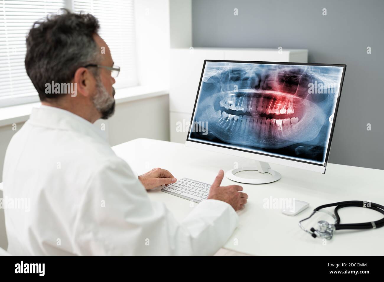 Mature Male Dentist Looking At Teeth X-ray On Computer In Clinic Stock ...