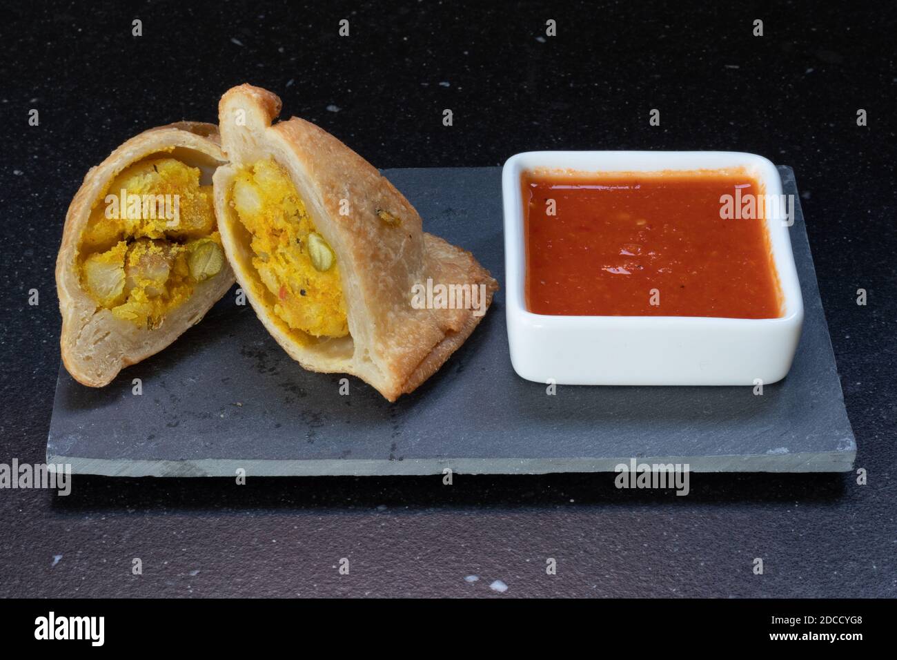 Modern Samosa serving with red hot sauce on a gray board and a dark ...