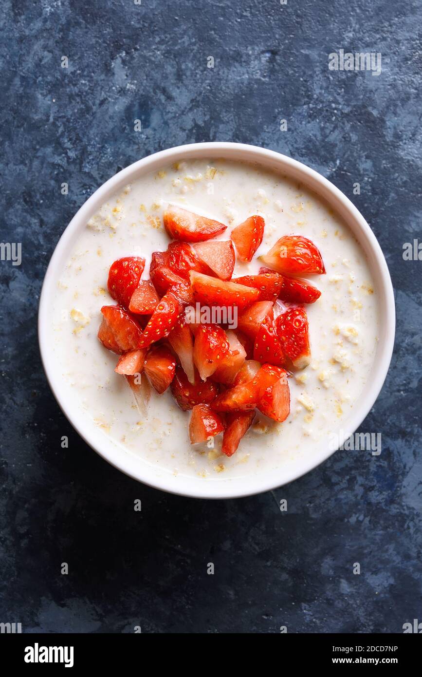 Close up view of oats porridge with strawberry in bowl over blue stone ...