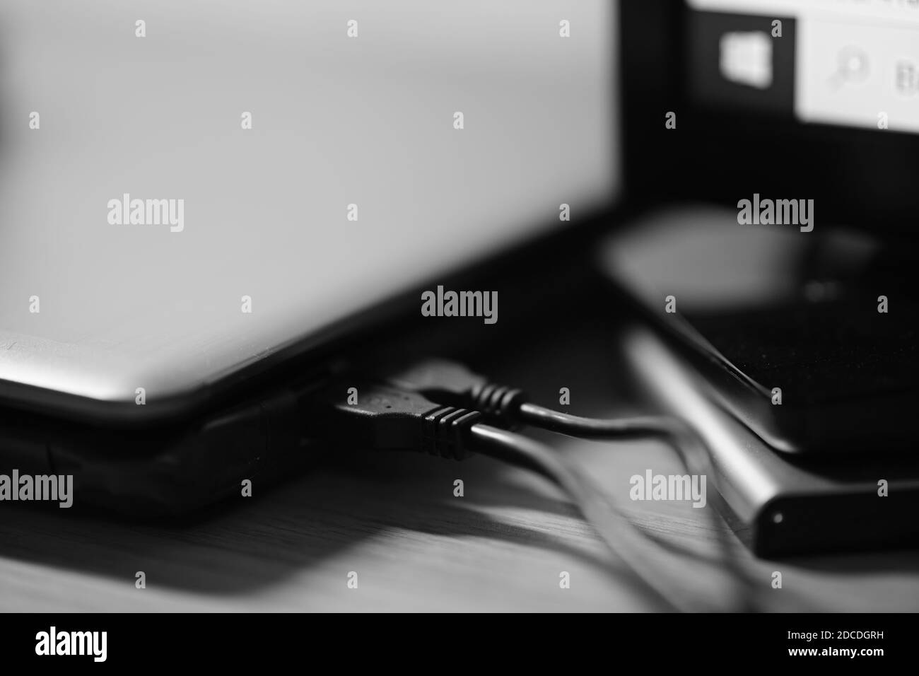 Part of a silver laptop with usb wires on a wooden table. Side view. BW ...