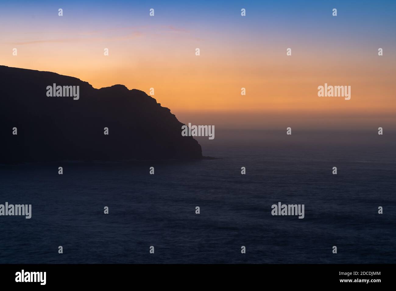 A sunrise over the ocean with cliff in silhouette and beautiful colors ...