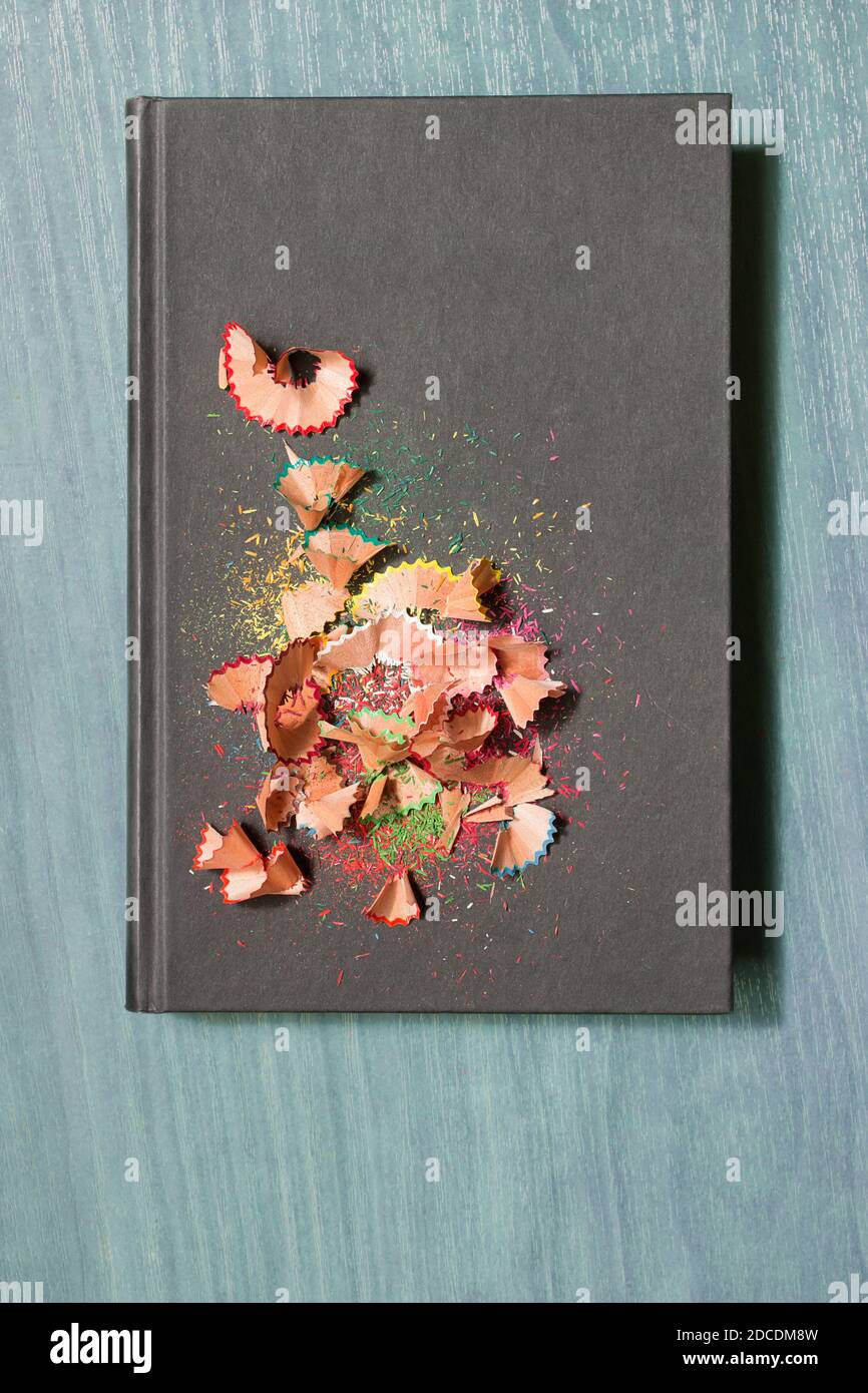 Black hardcover book with pieces of colored pencils on a blue wooden ...
