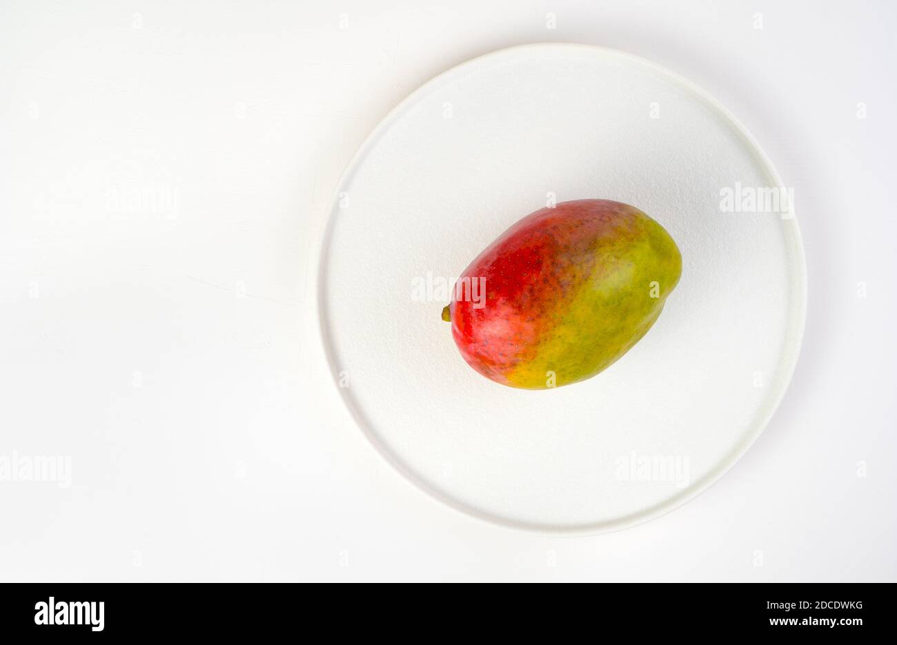 Mango lies on a white dish, unpeeled on a light background Stock Photo ...