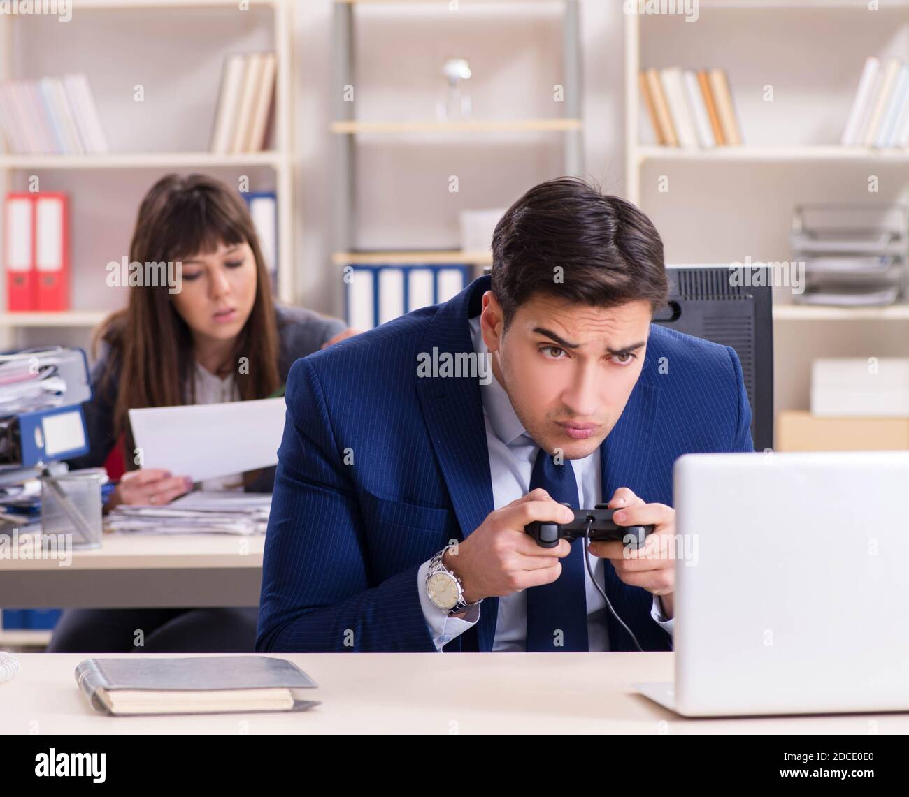 The man playing games in office while colleague is busy Stock Photo - Alamy