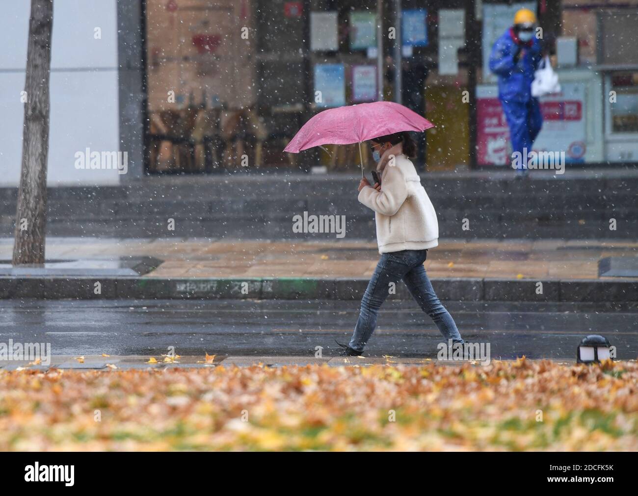 Beijing, China. 21st Nov, 2020. A woman walks on a street in snow in ...