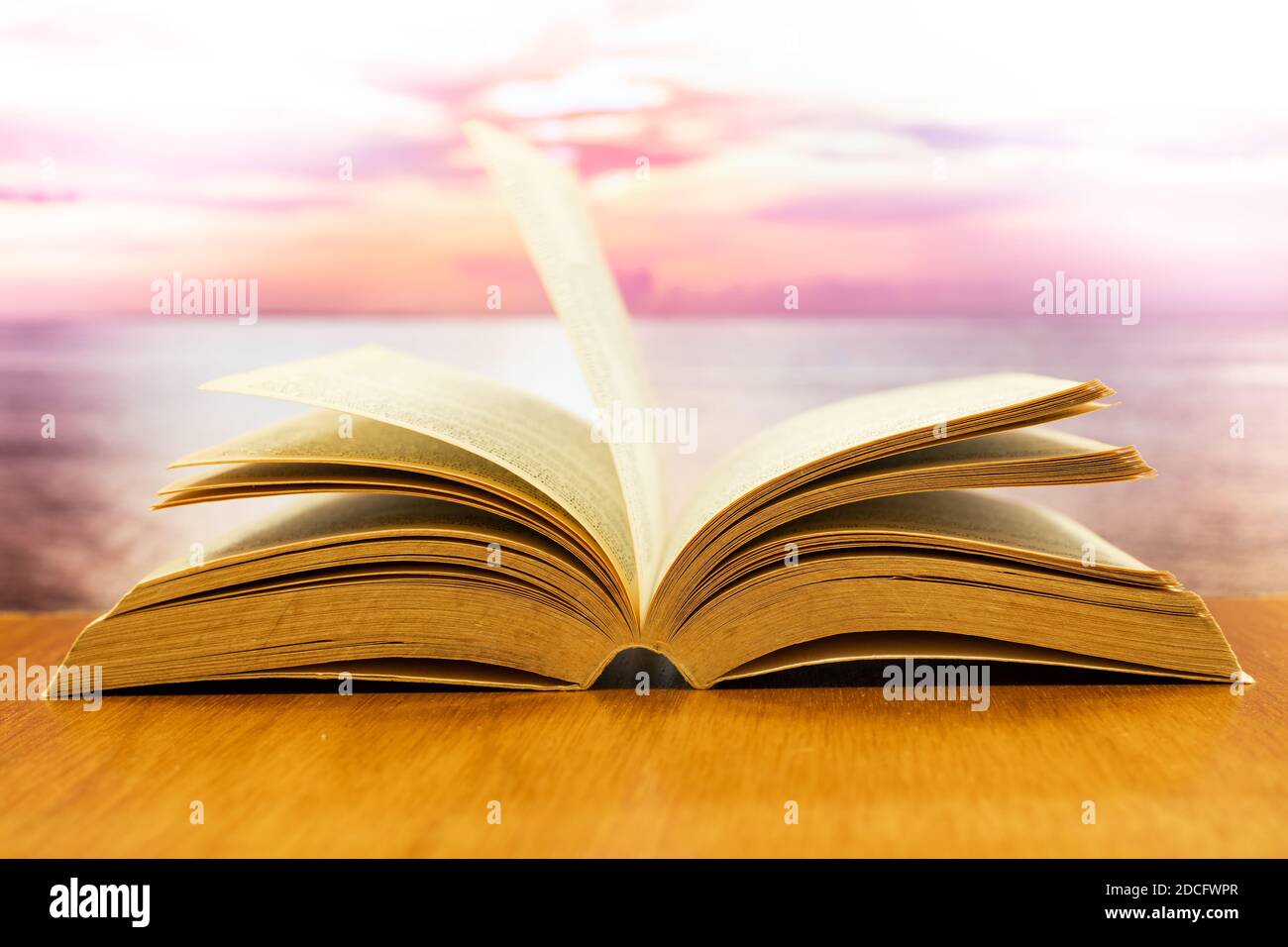 old book open on a wood table with blurred beautiful sunset in a calm ...