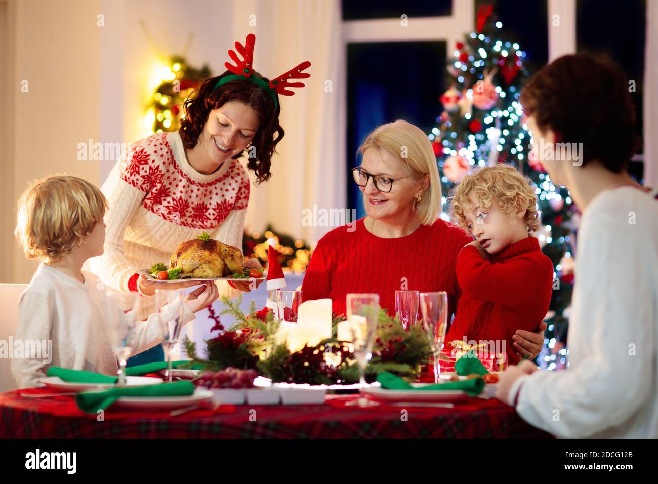 Family with children eating Christmas dinner at fireplace and decorated ...