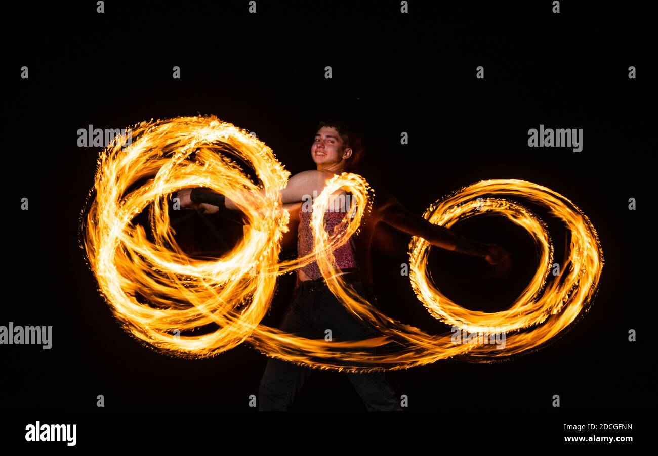 Happy male fire dancer twirl burning baton creating sparkling trails in ...