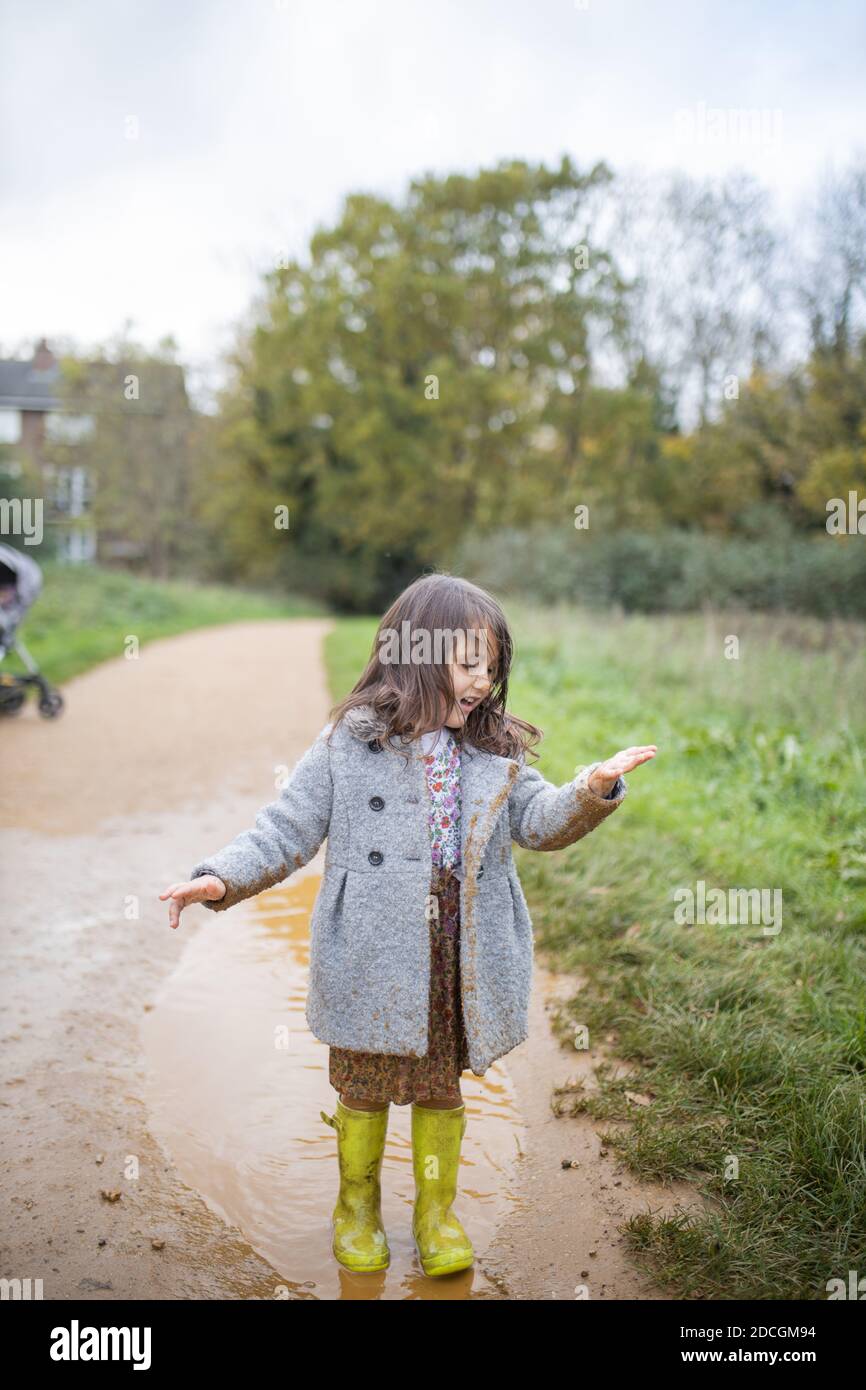 Little girl looking at her muddy clothes after jumping in a puddle ...