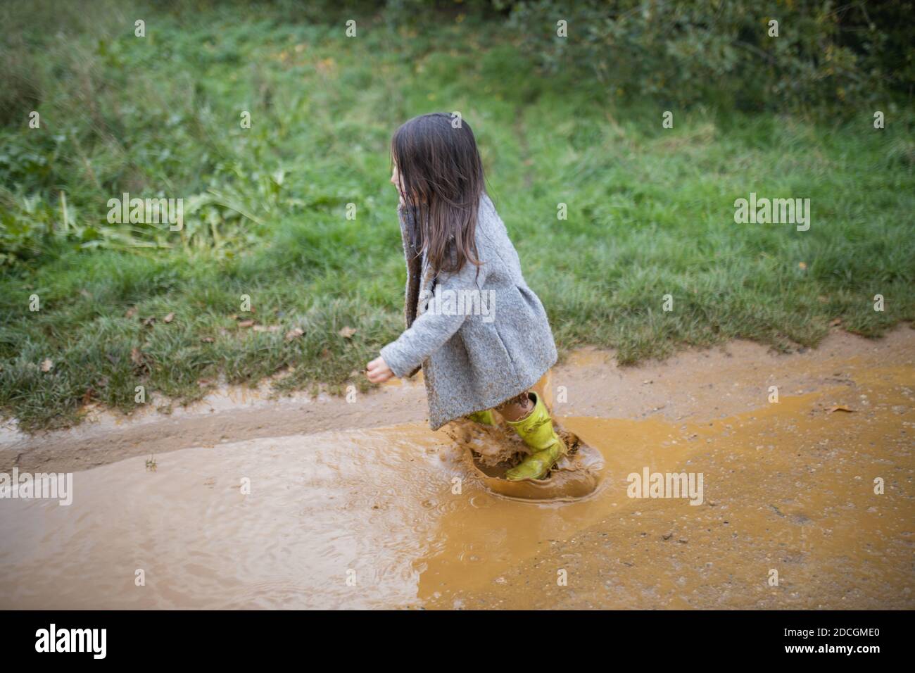 Happy little girl joyfully jumping and splashing in a muddy puddle ...
